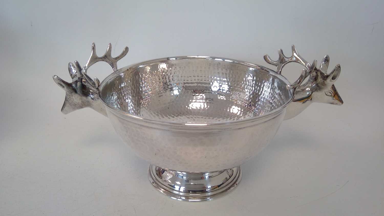 Lot 62 - A metal hammered bowl with stag head handles,